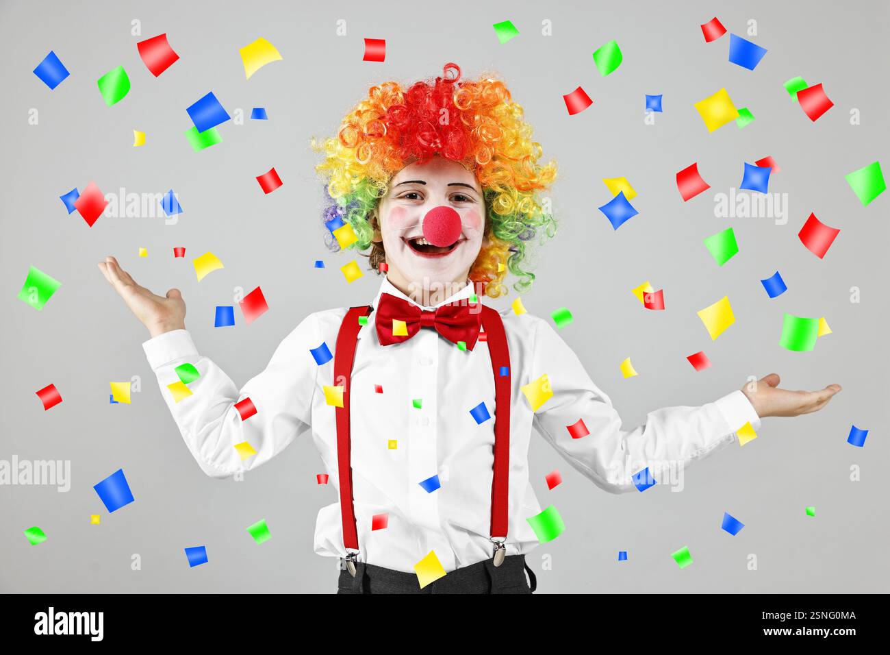 Happy boy dressed like clown under falling confetti on grey background ...