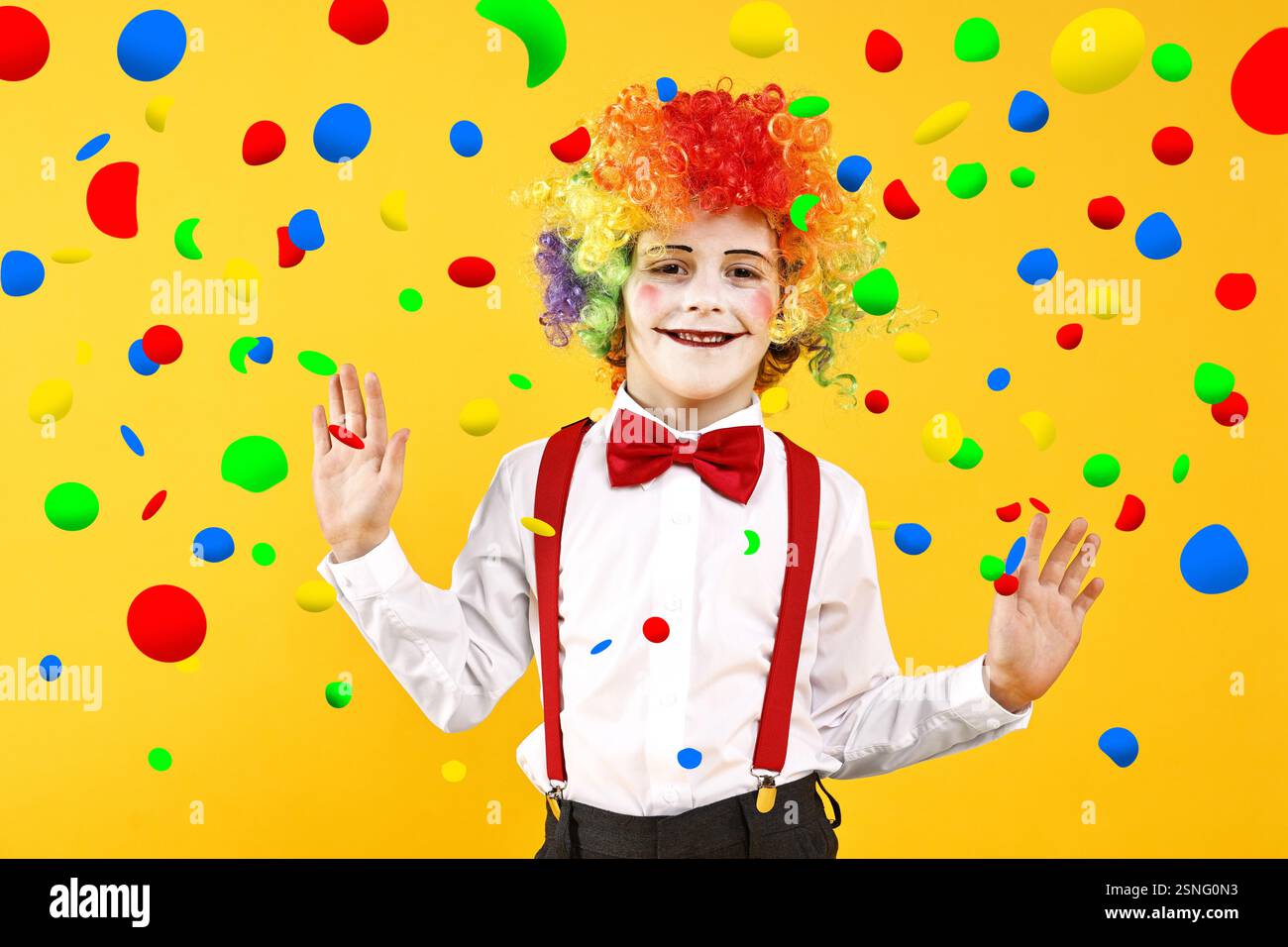 Happy boy dressed like clown under falling confetti on orange ...