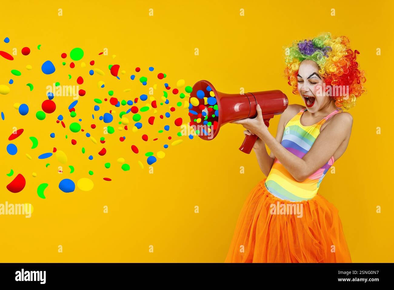 Cute girl dressed like clown shouting in megaphone with confetti flying ...
