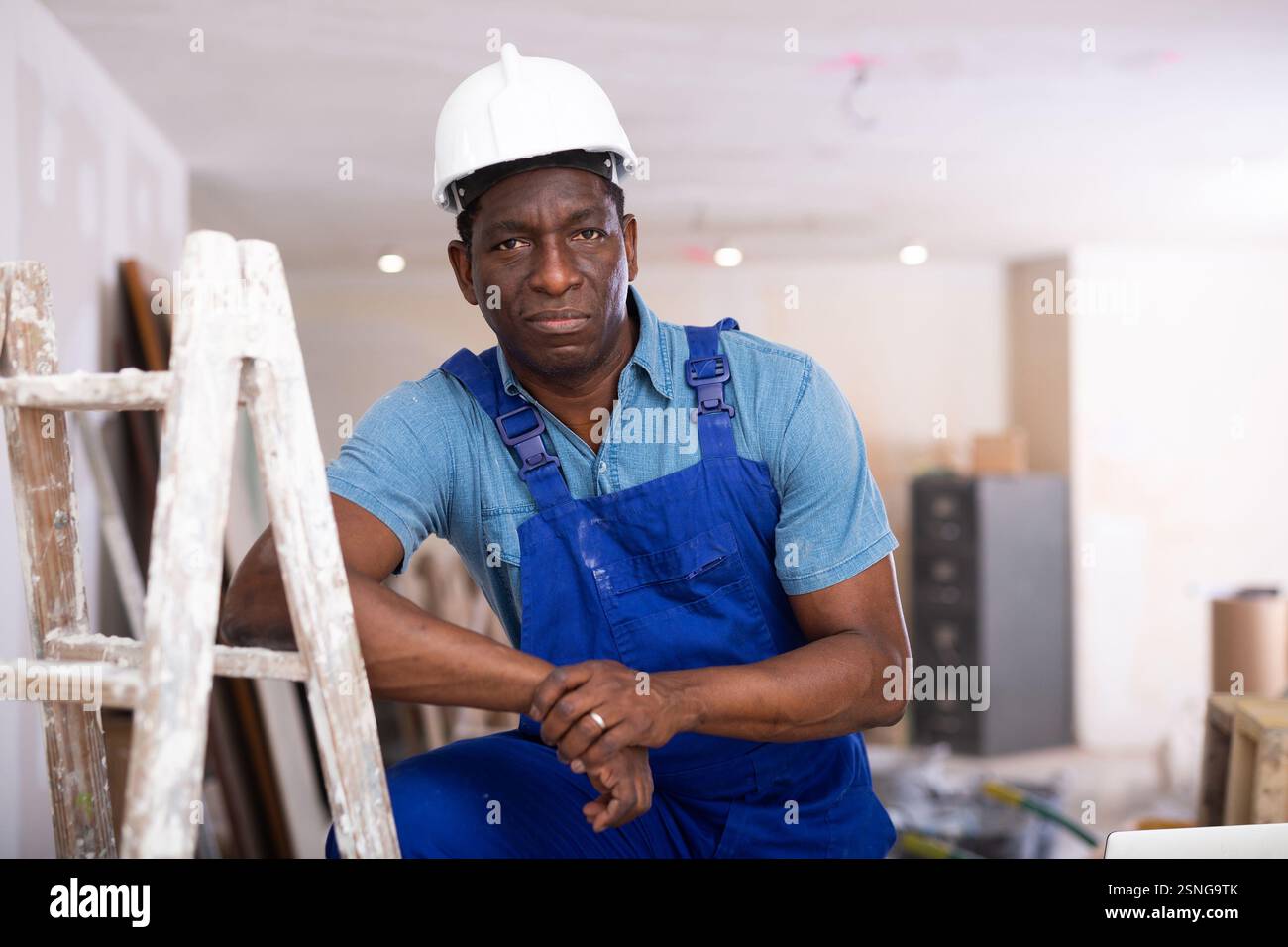 Portrait of confident african-american worker in blue overalls in room ...