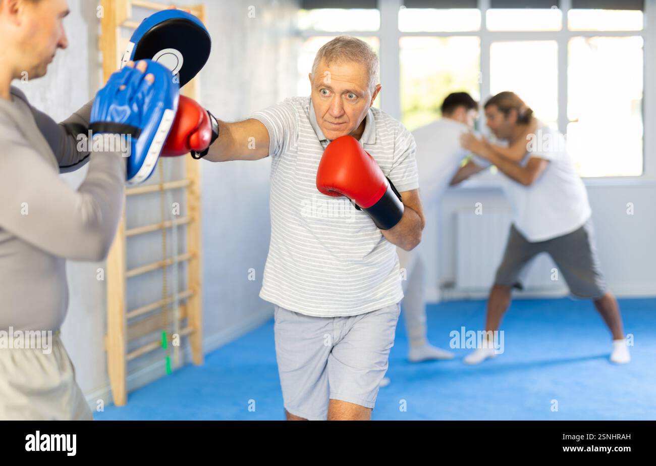Mature man works out strength and speed of boxing punch mitts with help ...
