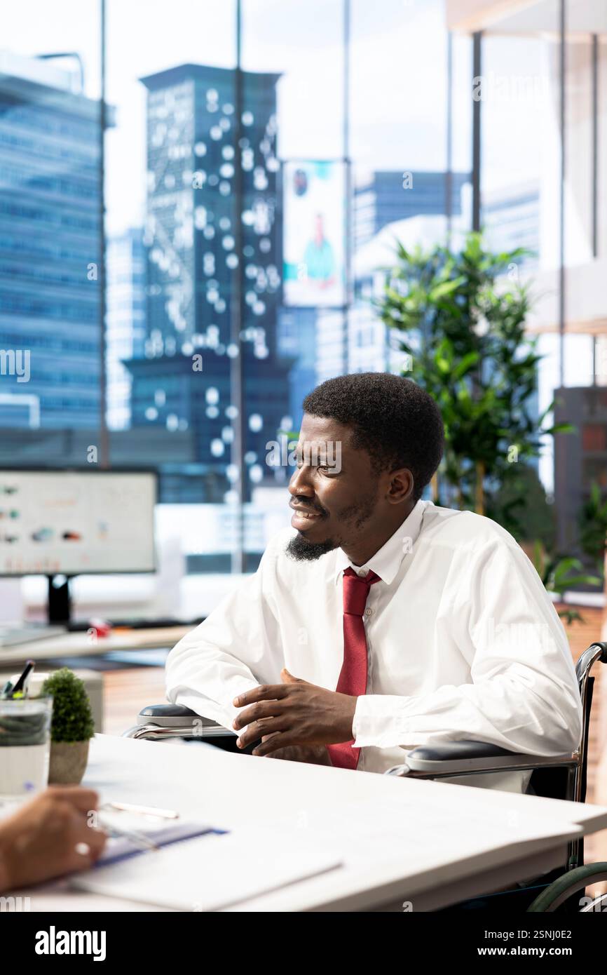 Cheerful employee in wheelchair, working together with colleagues in ...
