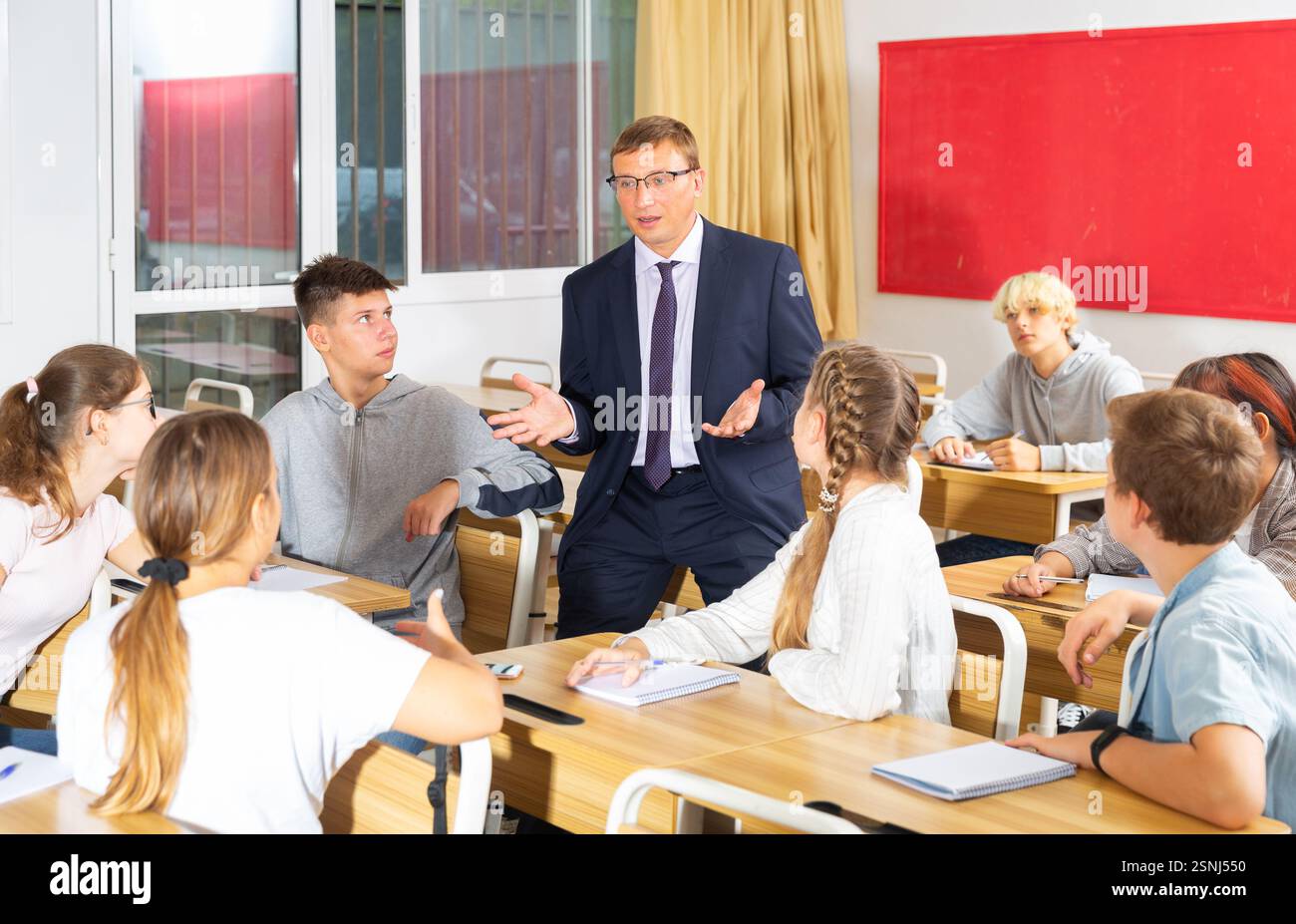 Friendly male teacher working with teen students in classroom Stock ...
