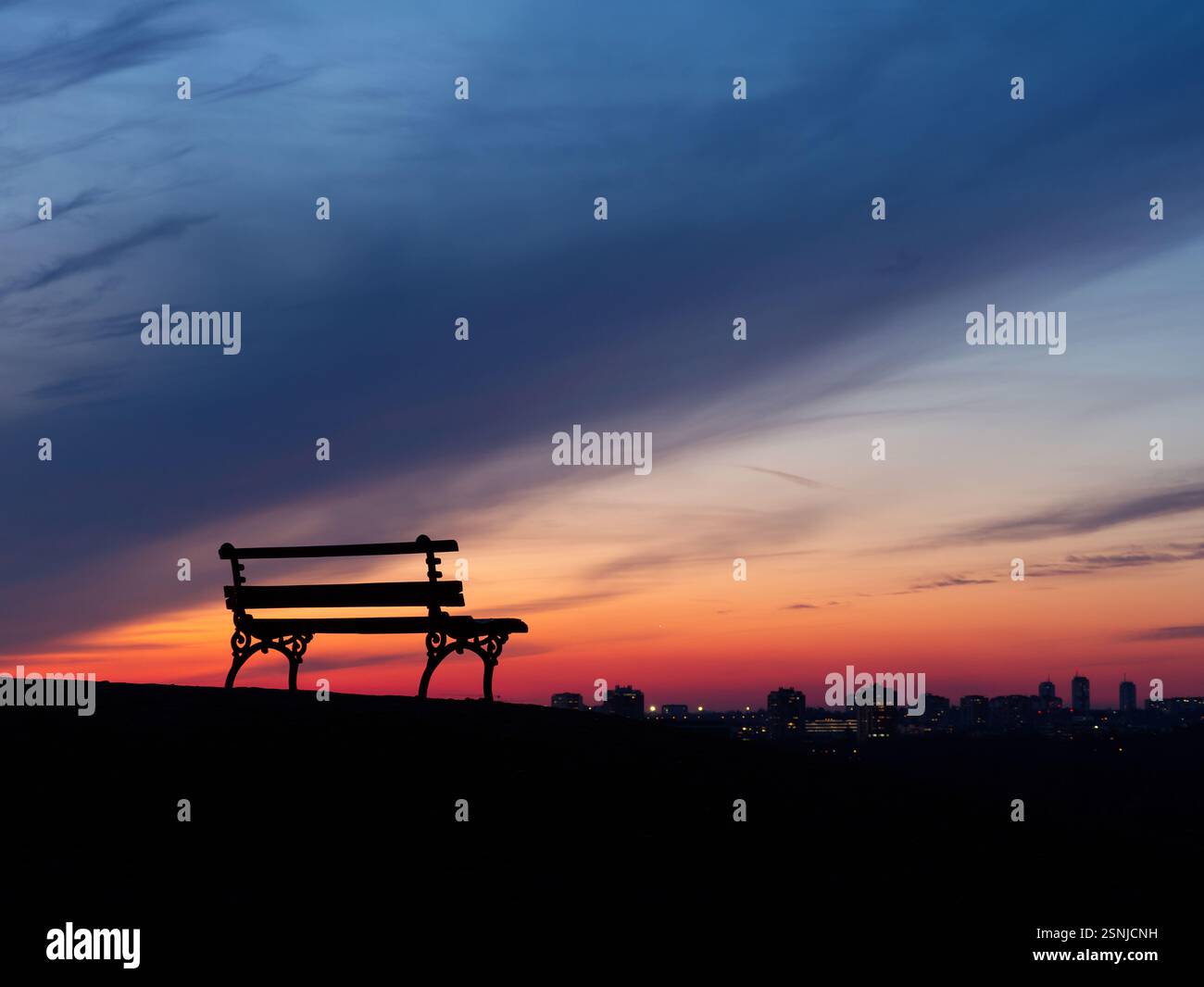 Silhouette of park bench against colorful sky with urban skyline in ...