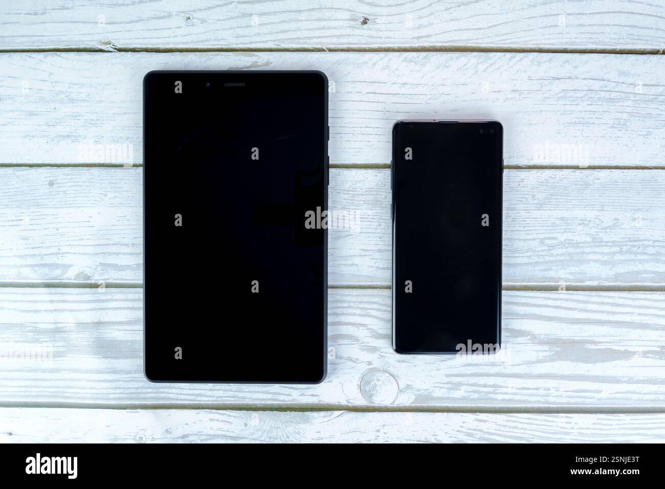 Black tablet and smartphone with turned-off screens placed side by side ...