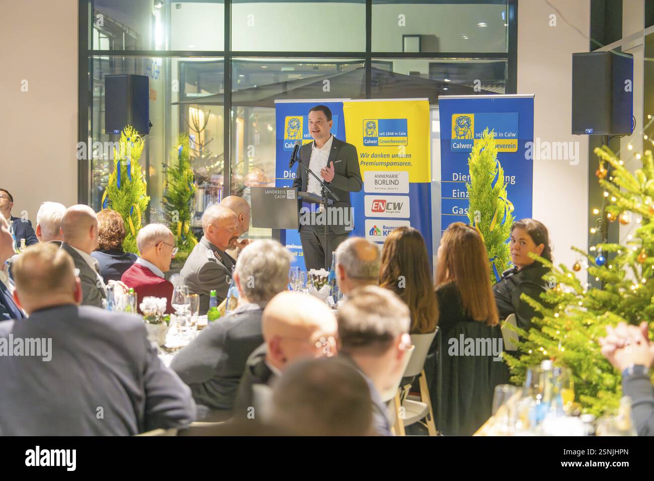 A speaker addresses a group of people at an event in a decorated room ...