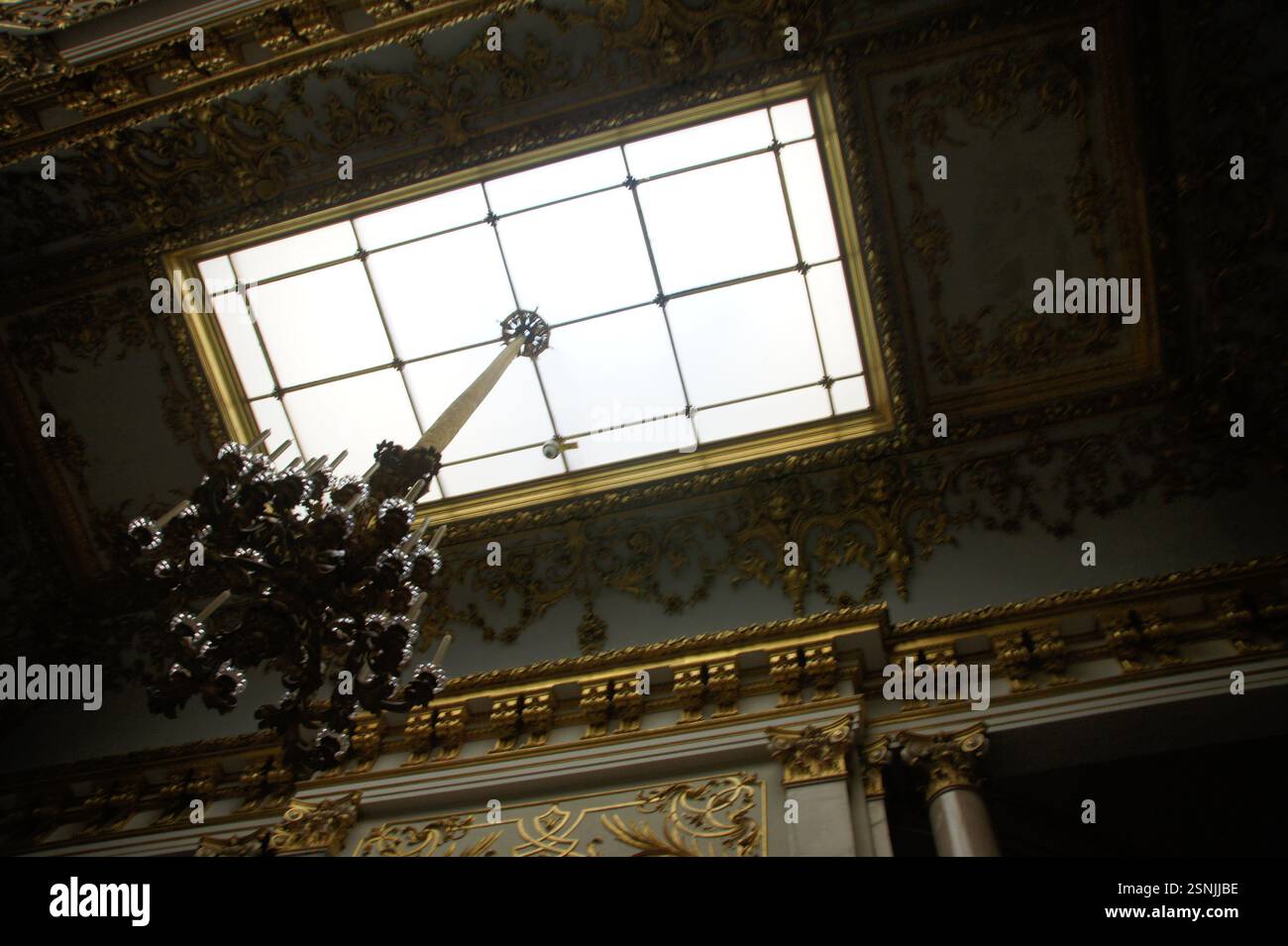 A crystal chandelier hangs from a decorated ceiling, casting elegant ...