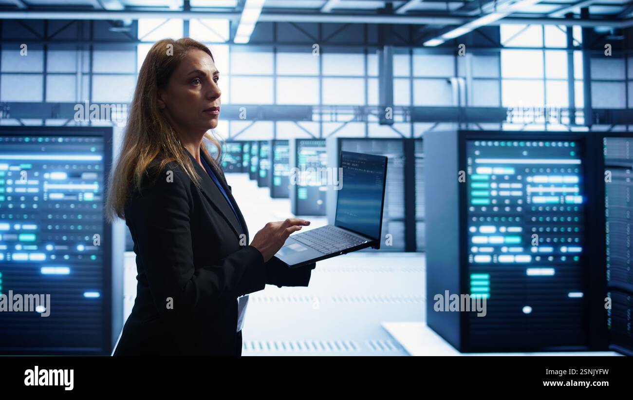 Woman walking in high tech facility, using laptop to patch network issues leading to slow data ...