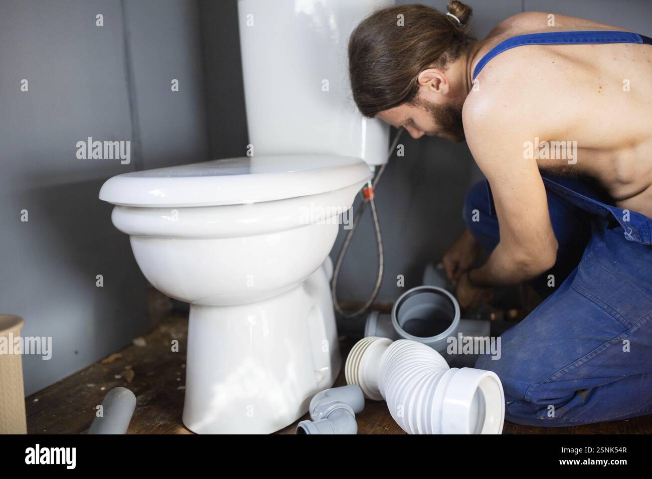 A man in overalls working on pipes near a toilet in a bathroom Stock ...