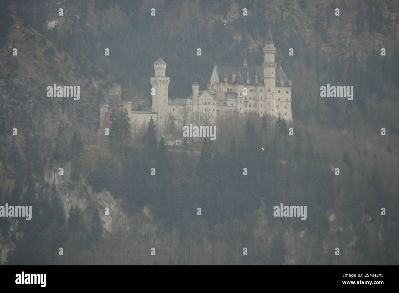 In Germany, Munich, a large white castle sits atop a forested mountain ...