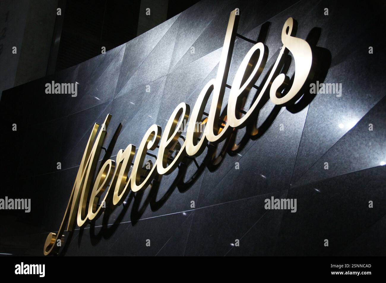 A gold Mercedes-Benz logo gleams on a black wall, signifying a luxury ...