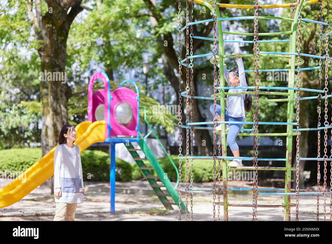 Childcare worker watching children playing on playground equipment ...