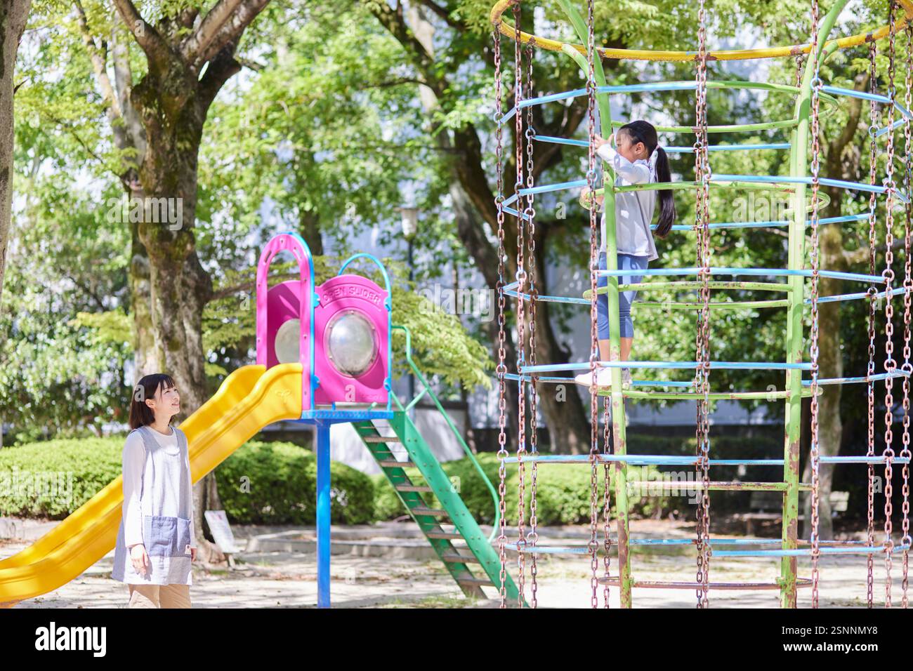 Childcare worker watching a child playing on the playground equipment ...