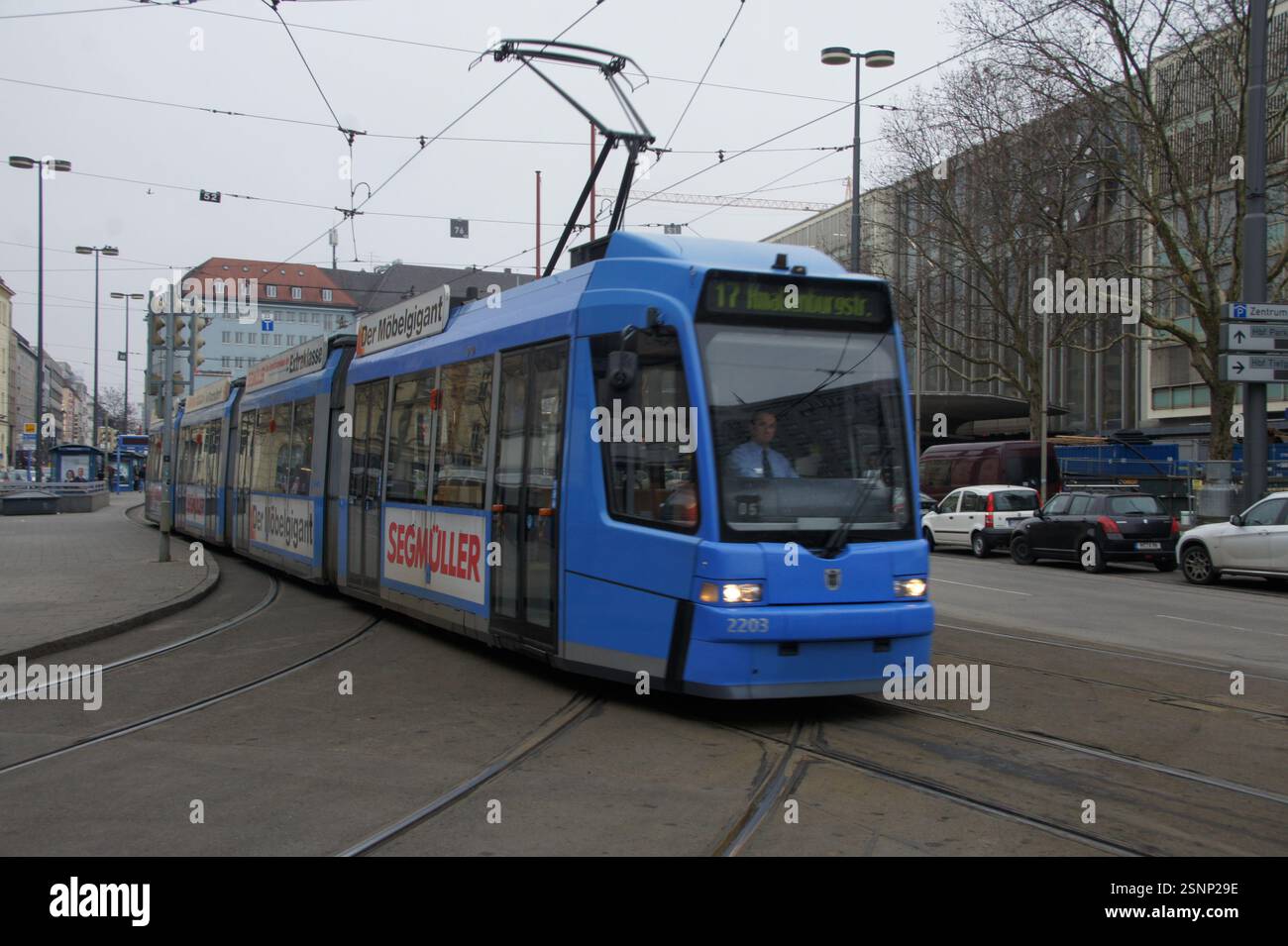 A blue and white Munich tram gracefully rounds a bend on a bustling ...