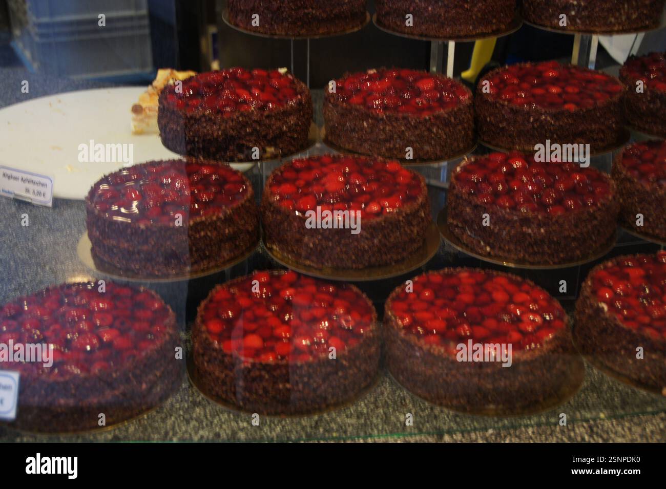 A display of delectable cakes in a bakery case, adorned with red ...