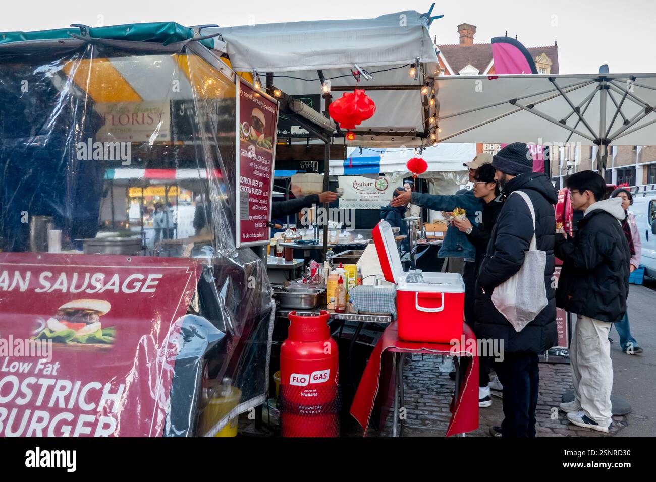 A busy street food vendor serves customers offering German sausage and ...