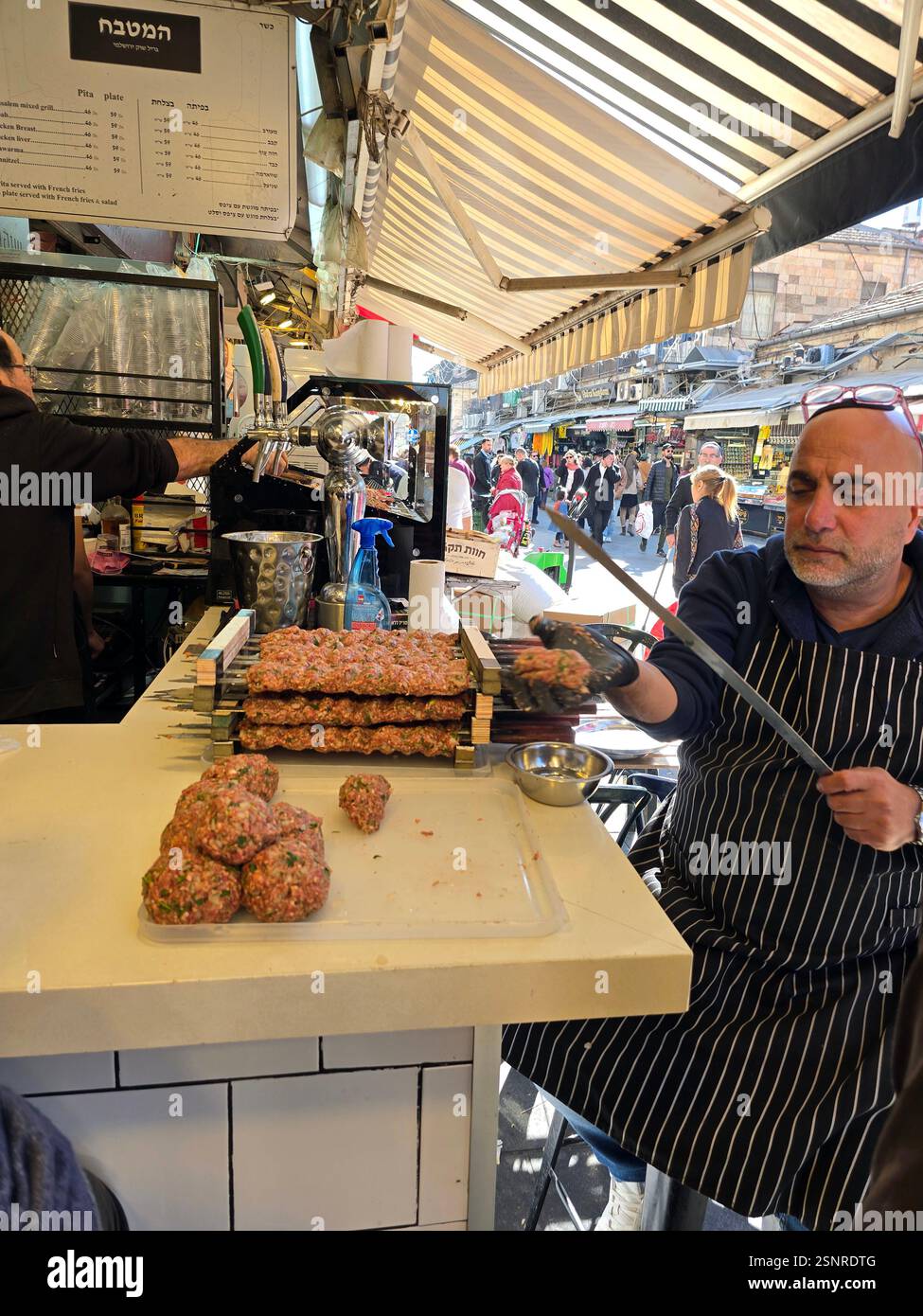 A cook expertly shapes seasoned meat for skewering amidst the lively ...