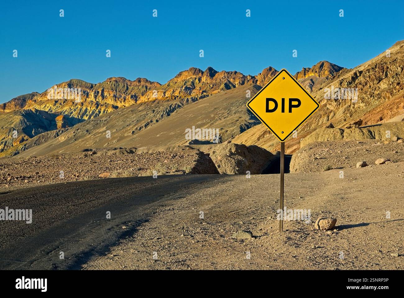 Road sign warning of ‘Dip’ along road through striated sandstone ...