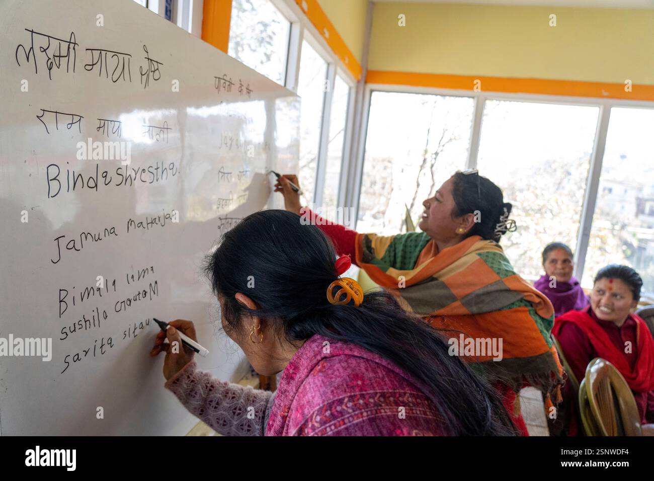 Women write their names on the board during a class at the Ujyalo ...