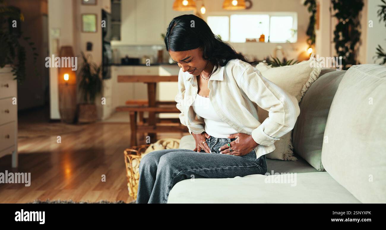 Woman, pain and stomach cramps on couch at house with period discomfort ...