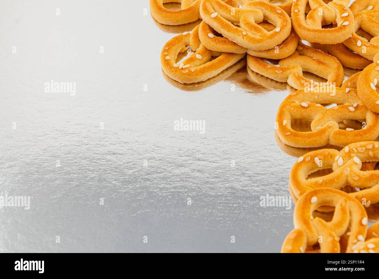 Golden pretzels are scattered across a shiny surface, emphasizing their ...