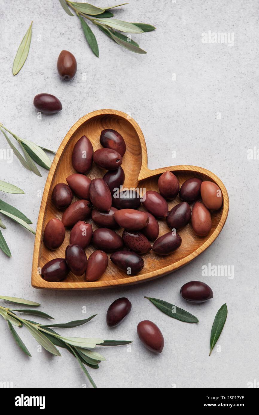 Olives in a heart shaped bowl with olive leaves on a gray background ...