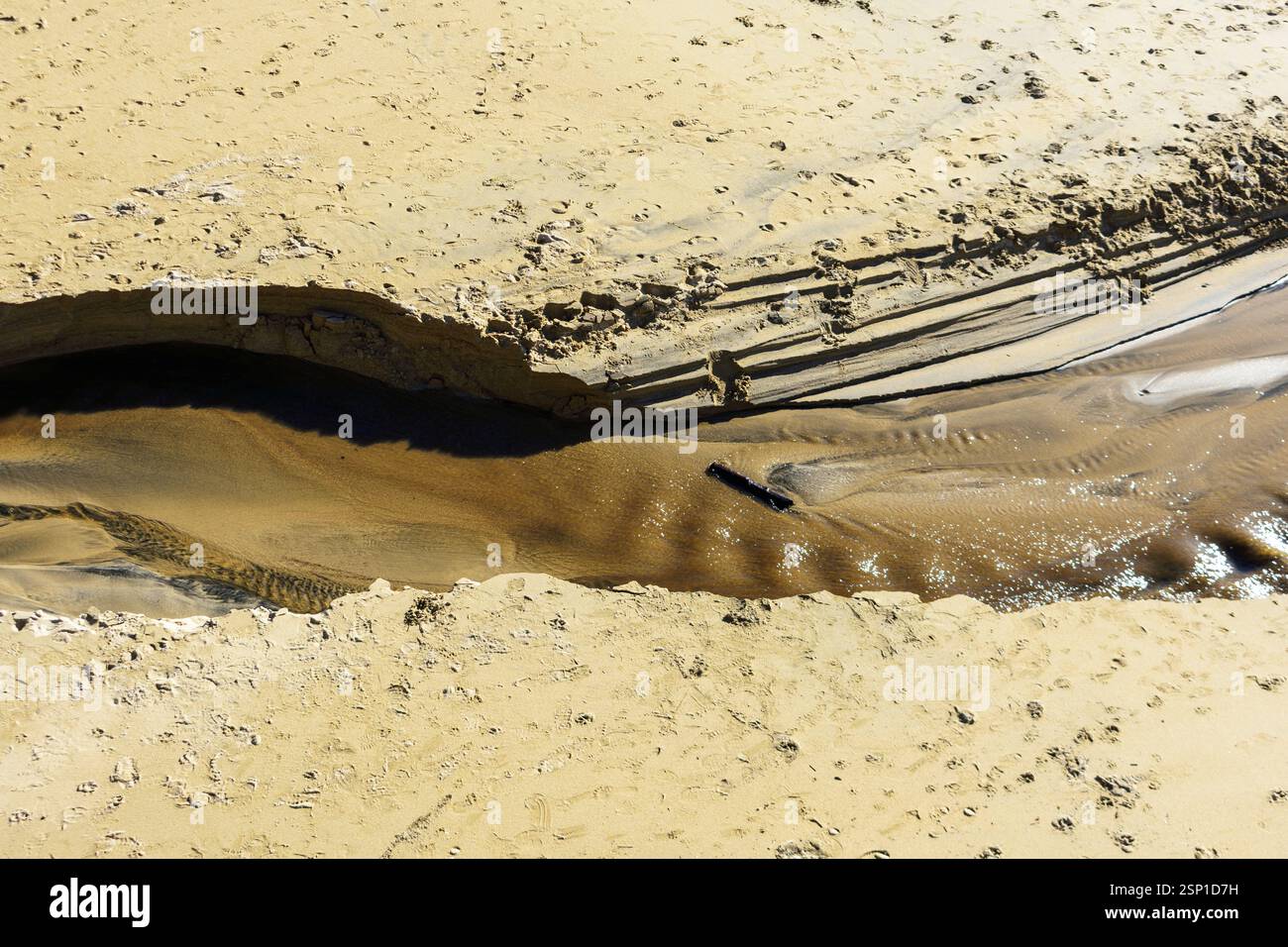 Shallow stream cuts through sandy terrain, revealing eroded edges and ...