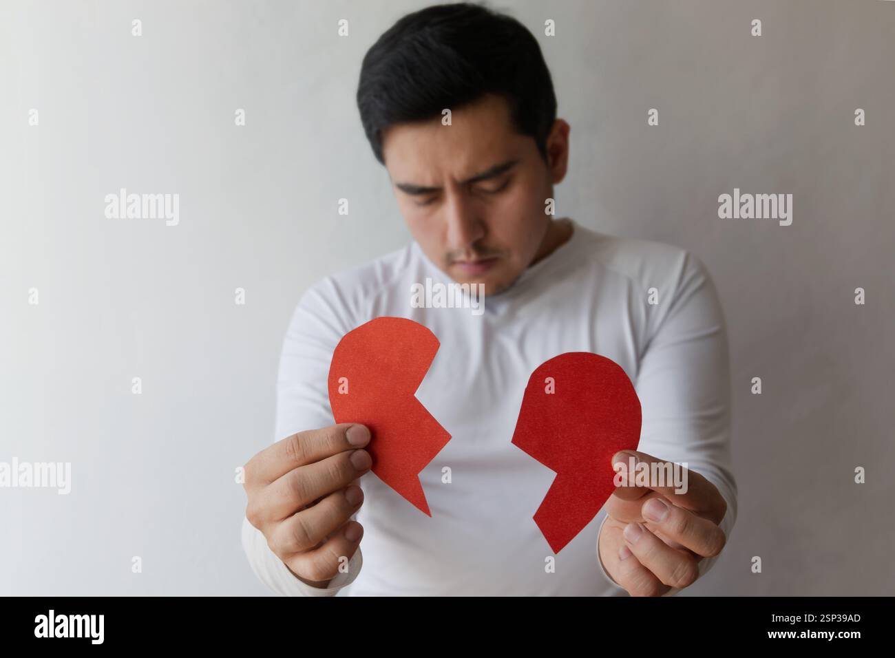 A young man with a serious expression holds two red paper hearts in his ...