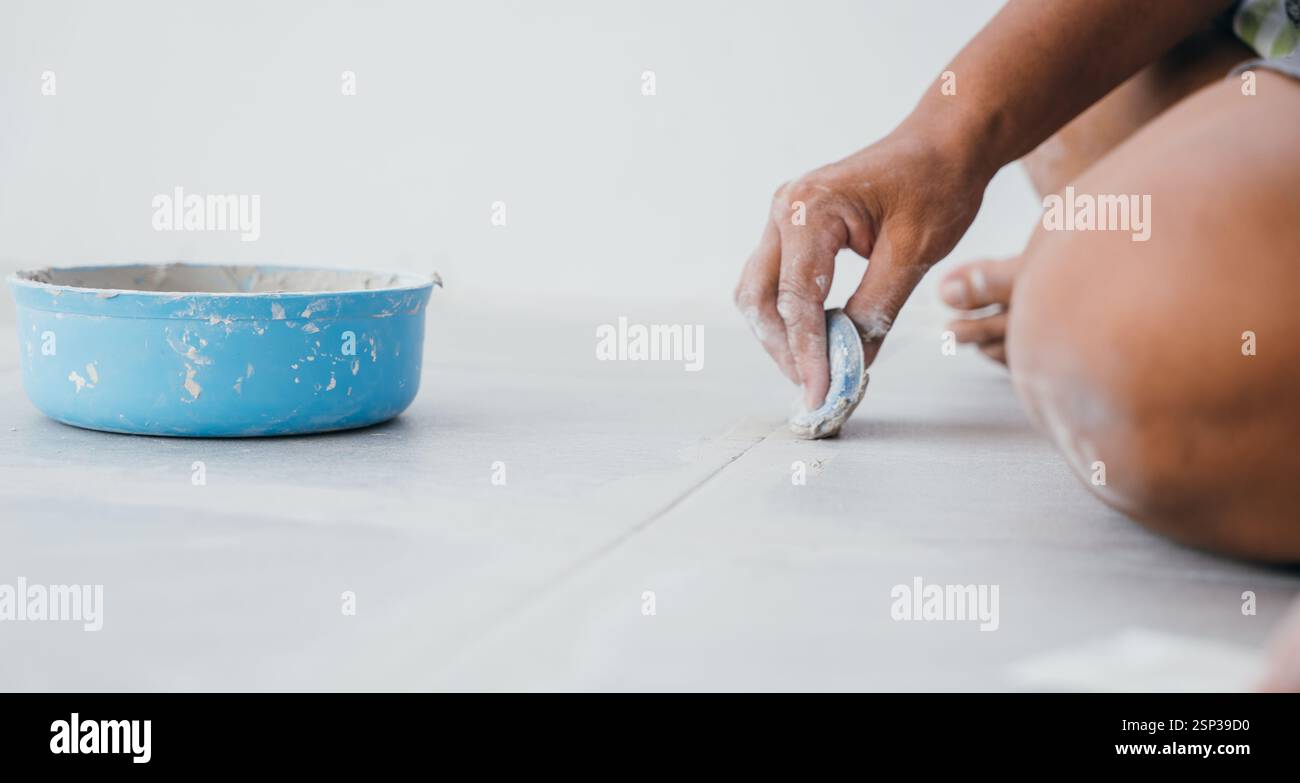 A hand with a rubber trowel smoothing mortar between gray ceramic floor ...