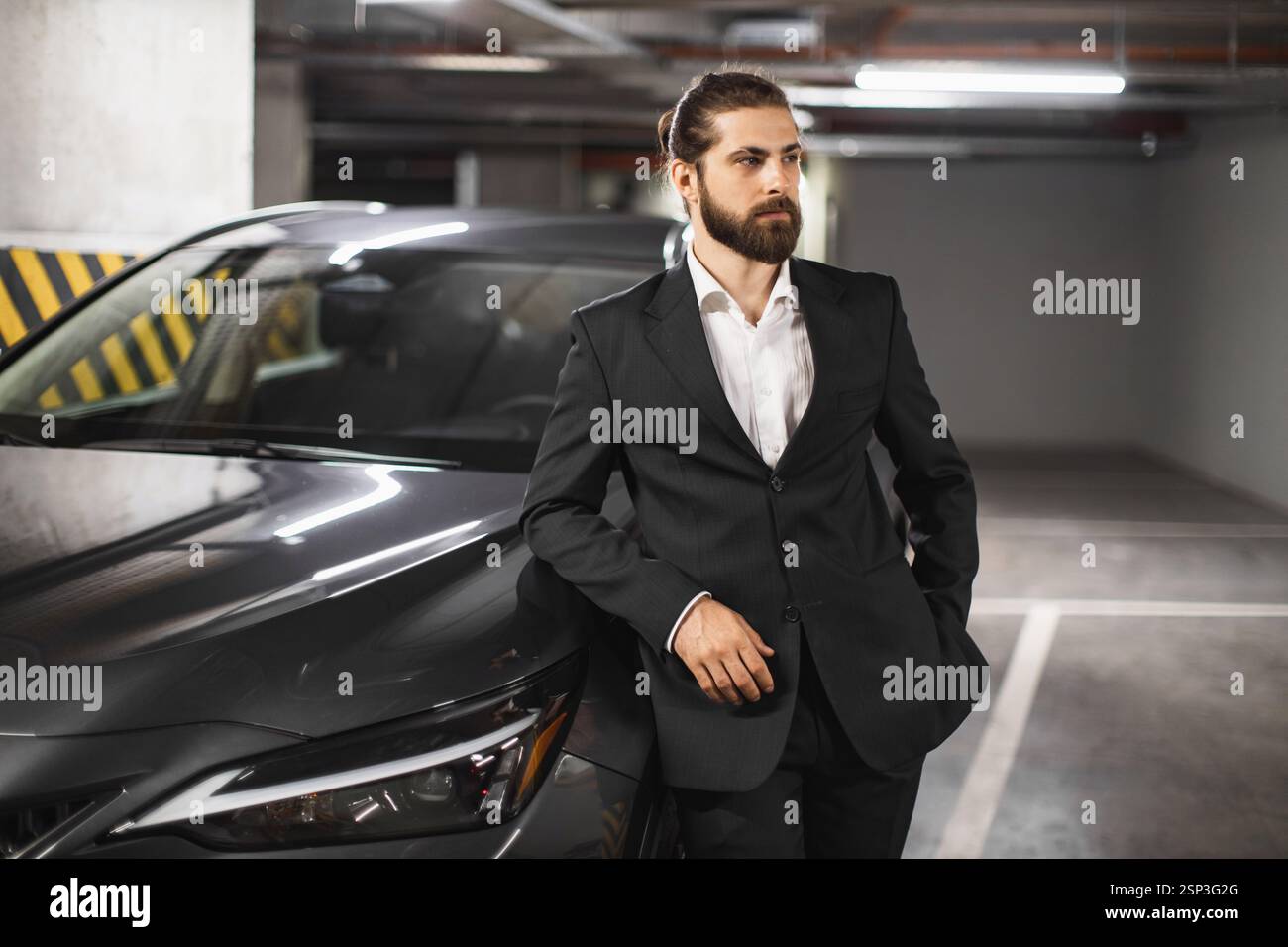 Young Caucasian man in formal suit leaning on car in underground ...