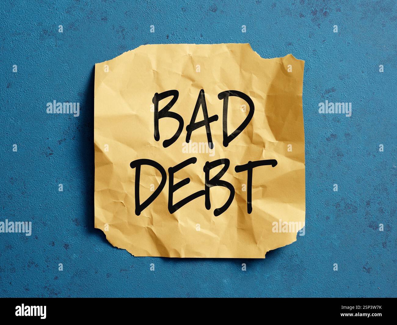 Crumpled yellow paper note with handwritten bad debt message over blue ...