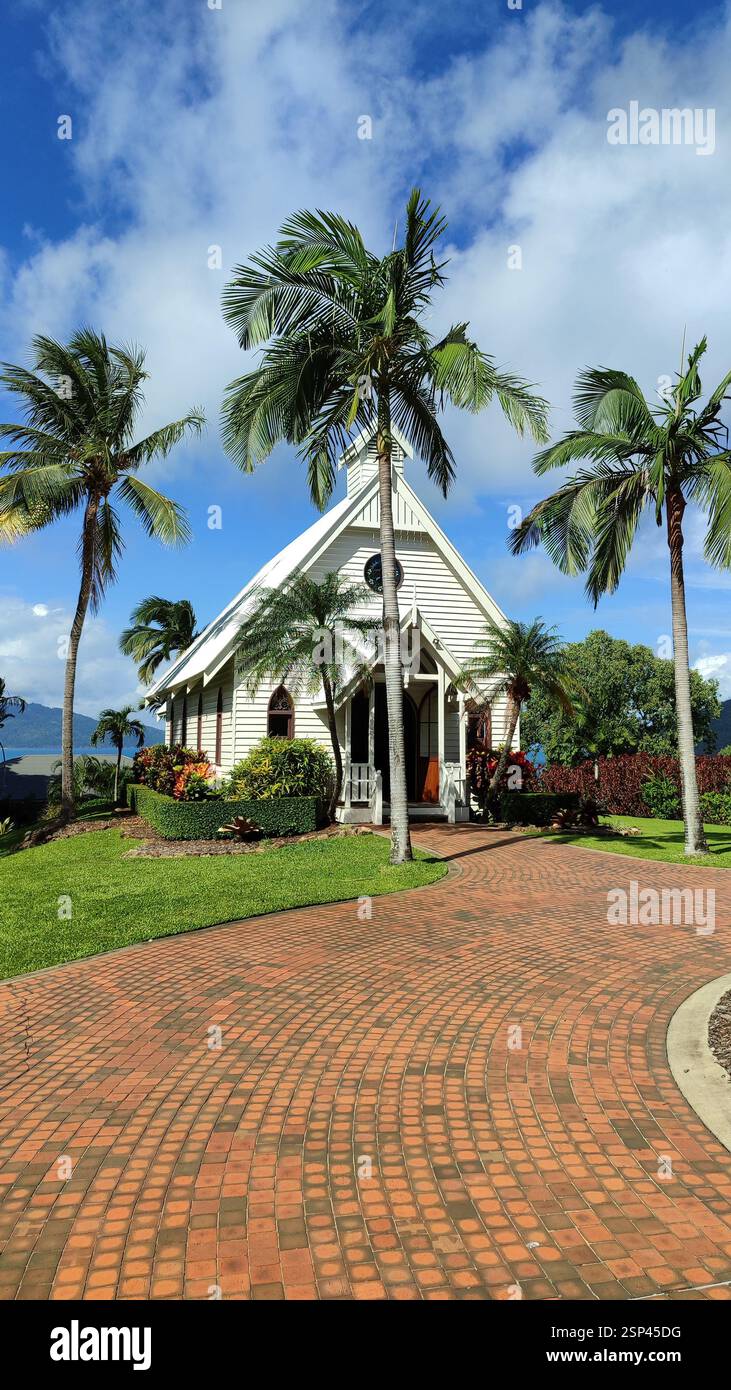 A small white church with a brick driveway is surrounded by palm trees ...