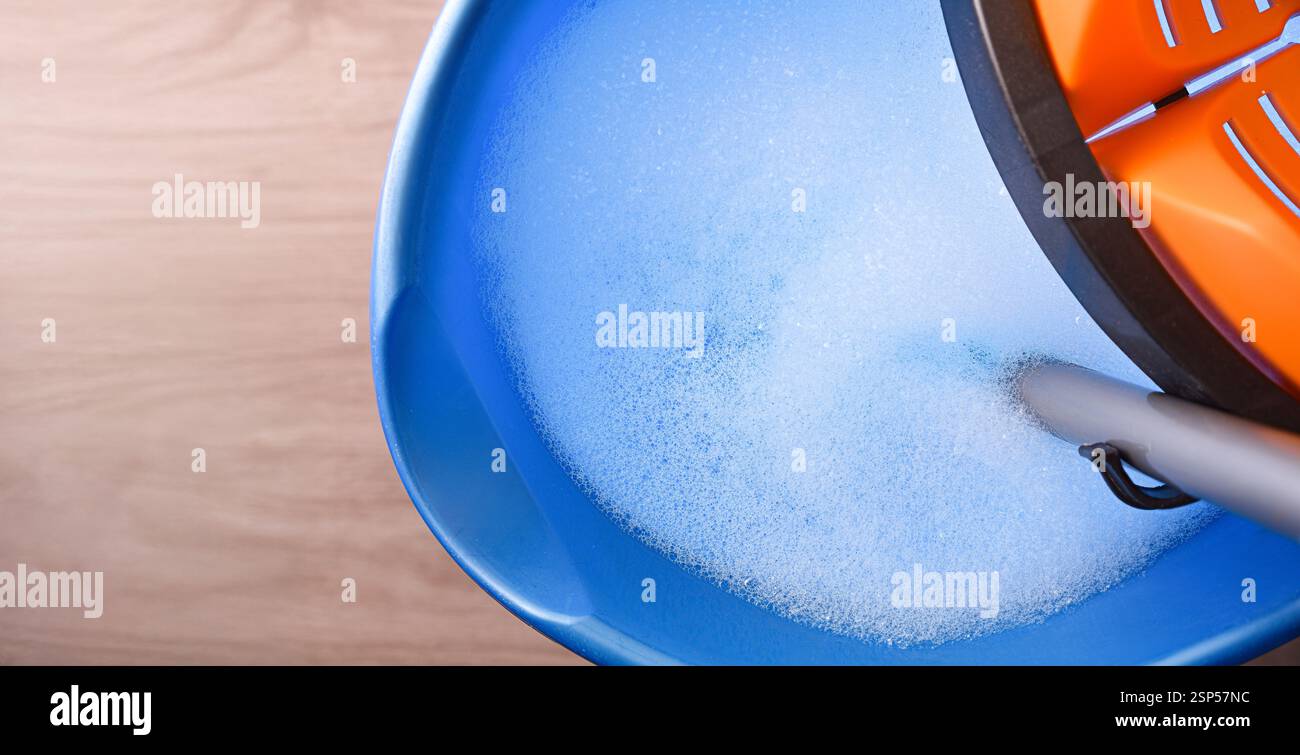 Detail of blue mop bucket filled with foamy water and grey mop handle ...