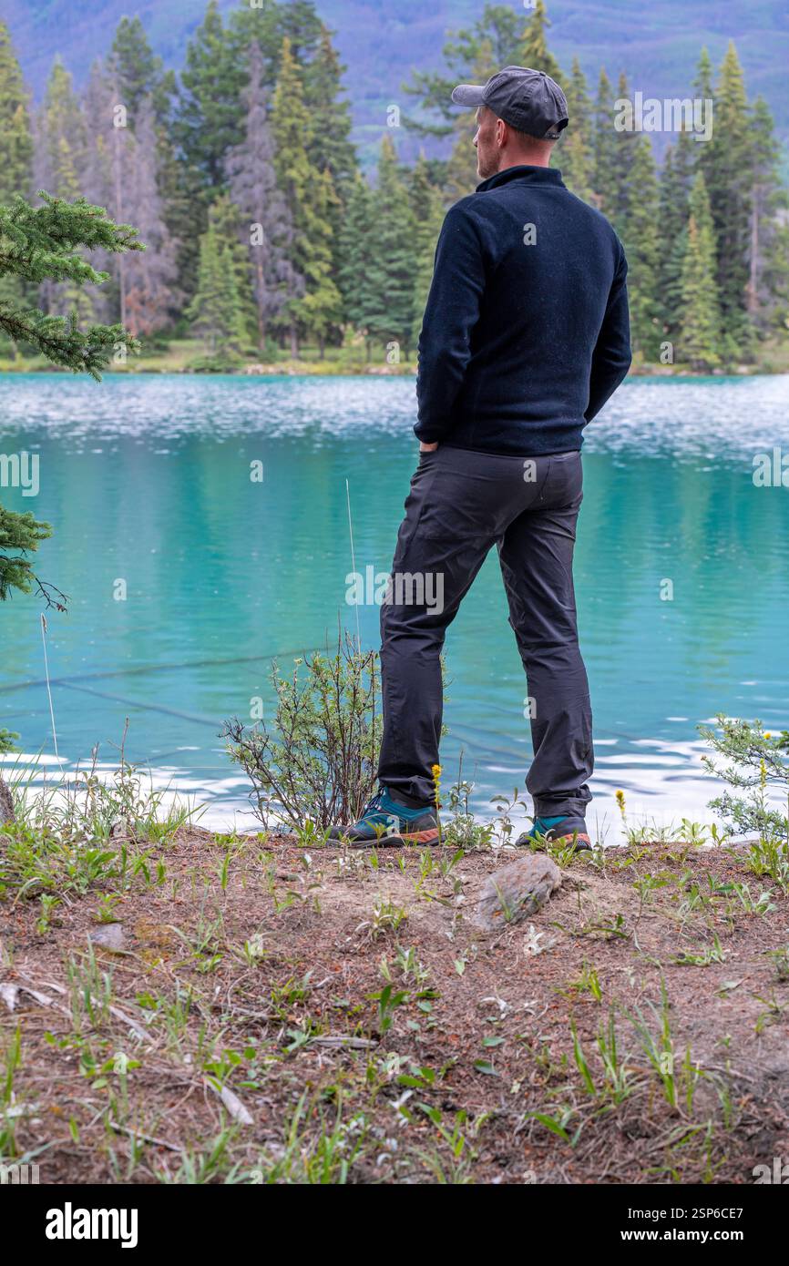 Young man hiker by Beauvert Lake looking at turquoise glacier waters of ...