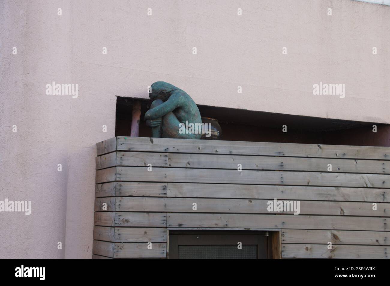 The small bronze sculpture depicts a hunched figure on a wooden balcony ...