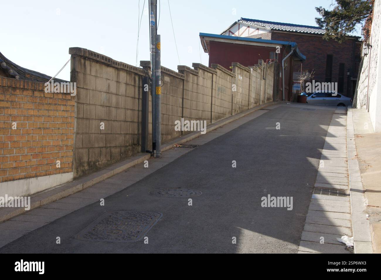 Sloped alleyway, South Korea. Tall brick wall on left, modern buildings ...