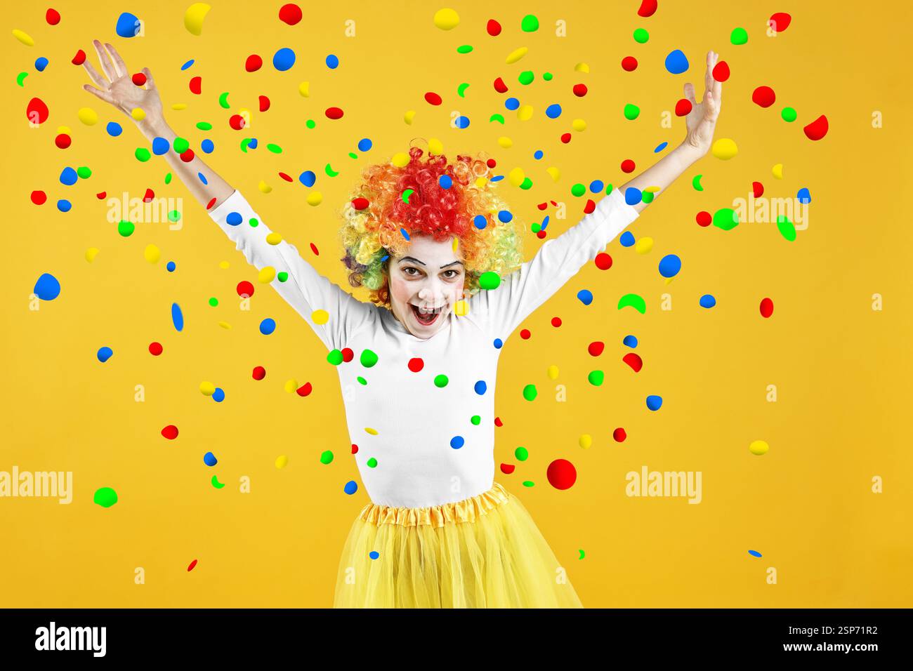 Happy girl dressed like clown under falling confetti on orange ...
