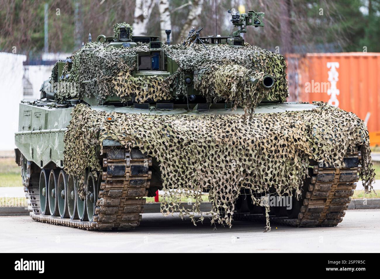 A German Leopard 2 main battle tank covered in camouflage netting, parked outdoors in a military ...