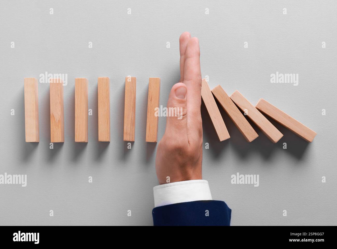 Man stopping wooden blocks from falling on grey background, top view ...