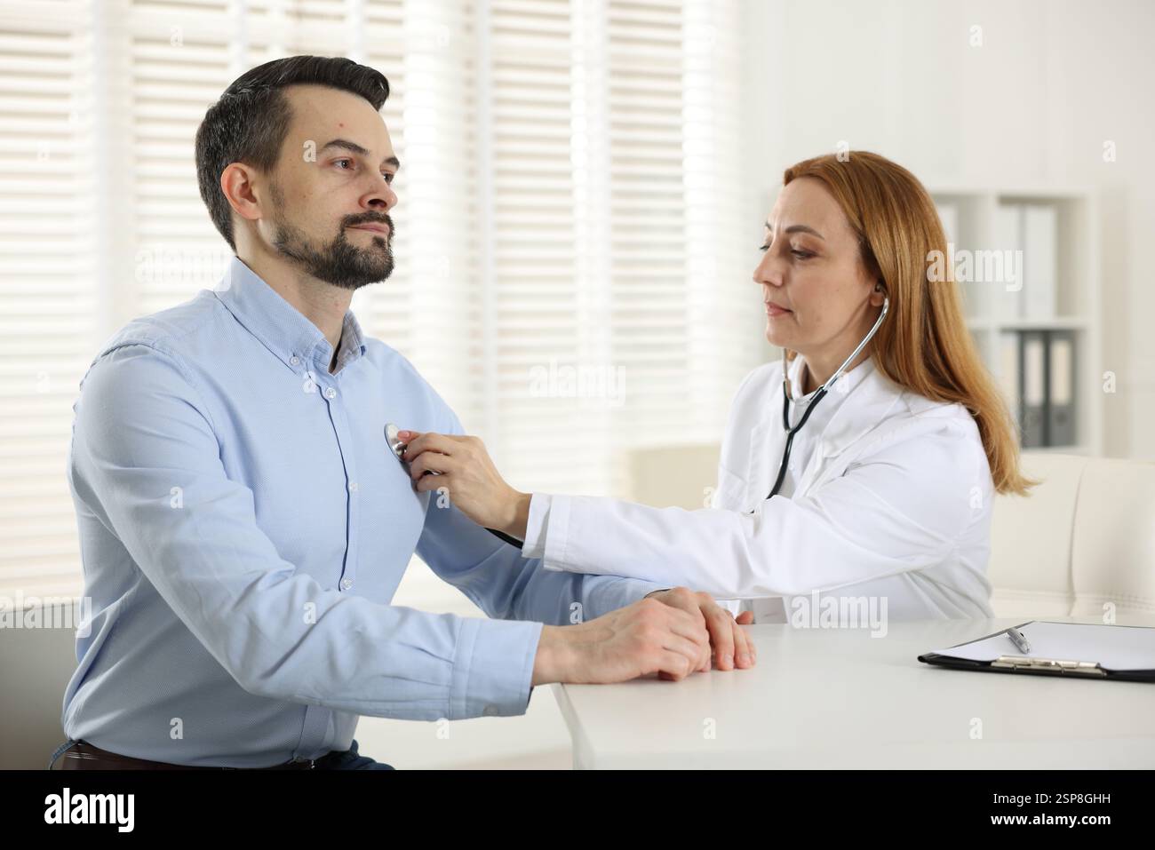 Cardiologist with stethoscope listening patient's heartbeat at desk in ...