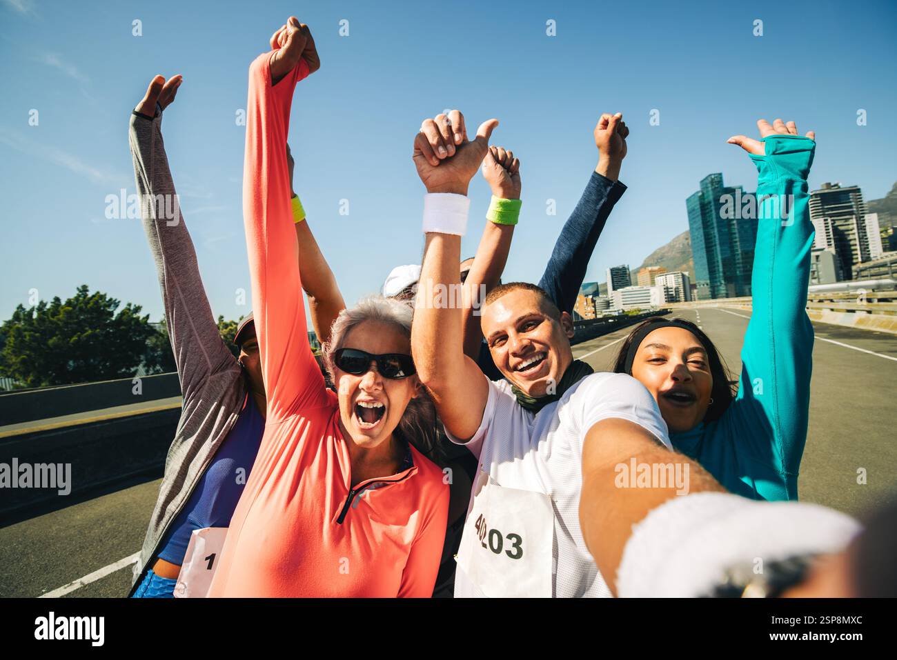 A group of diverse runners celebrates with raised arms after completing ...