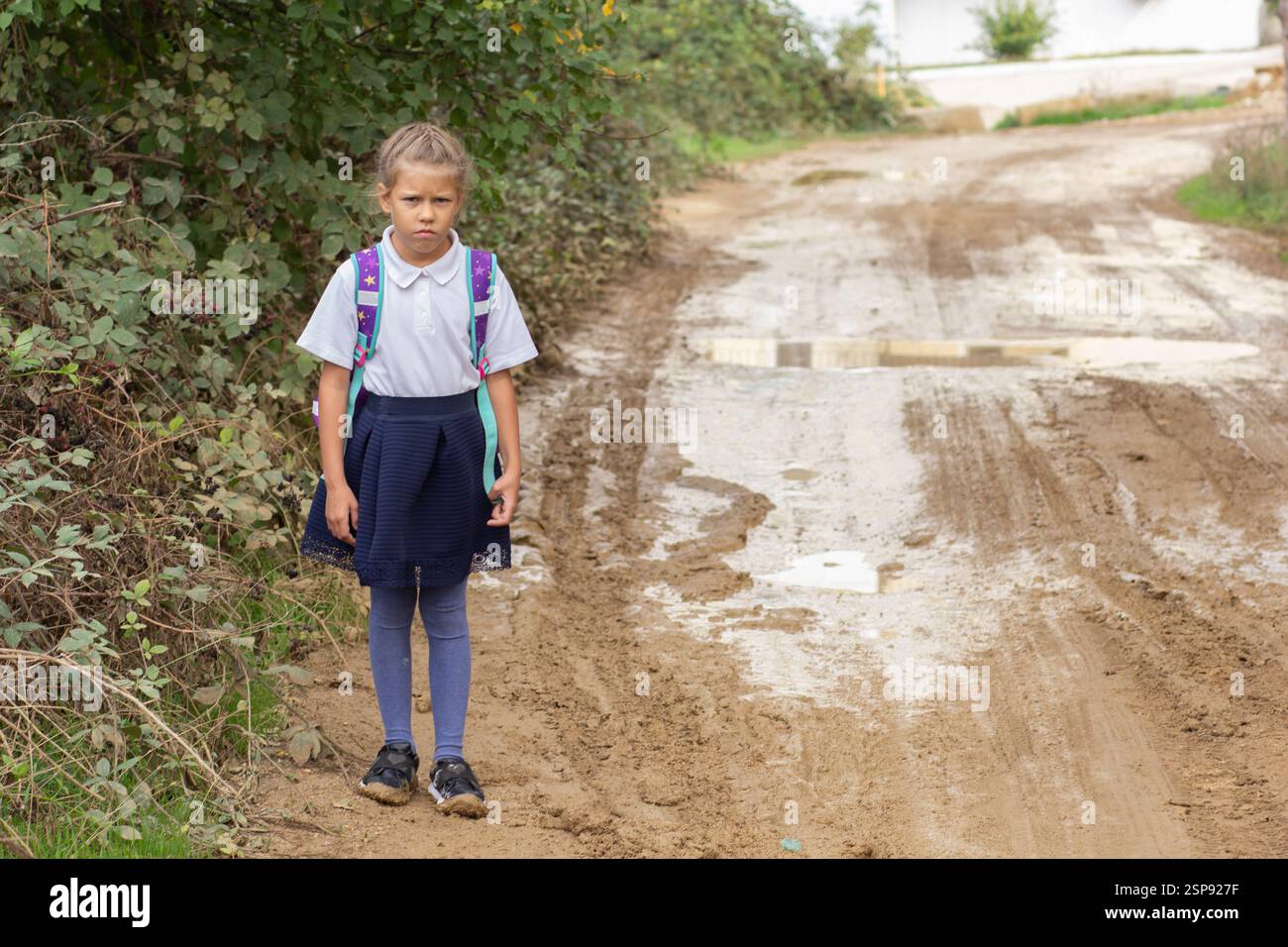 Sad caucasian child of 7 8 years with muddy shoes on dirty road going ...