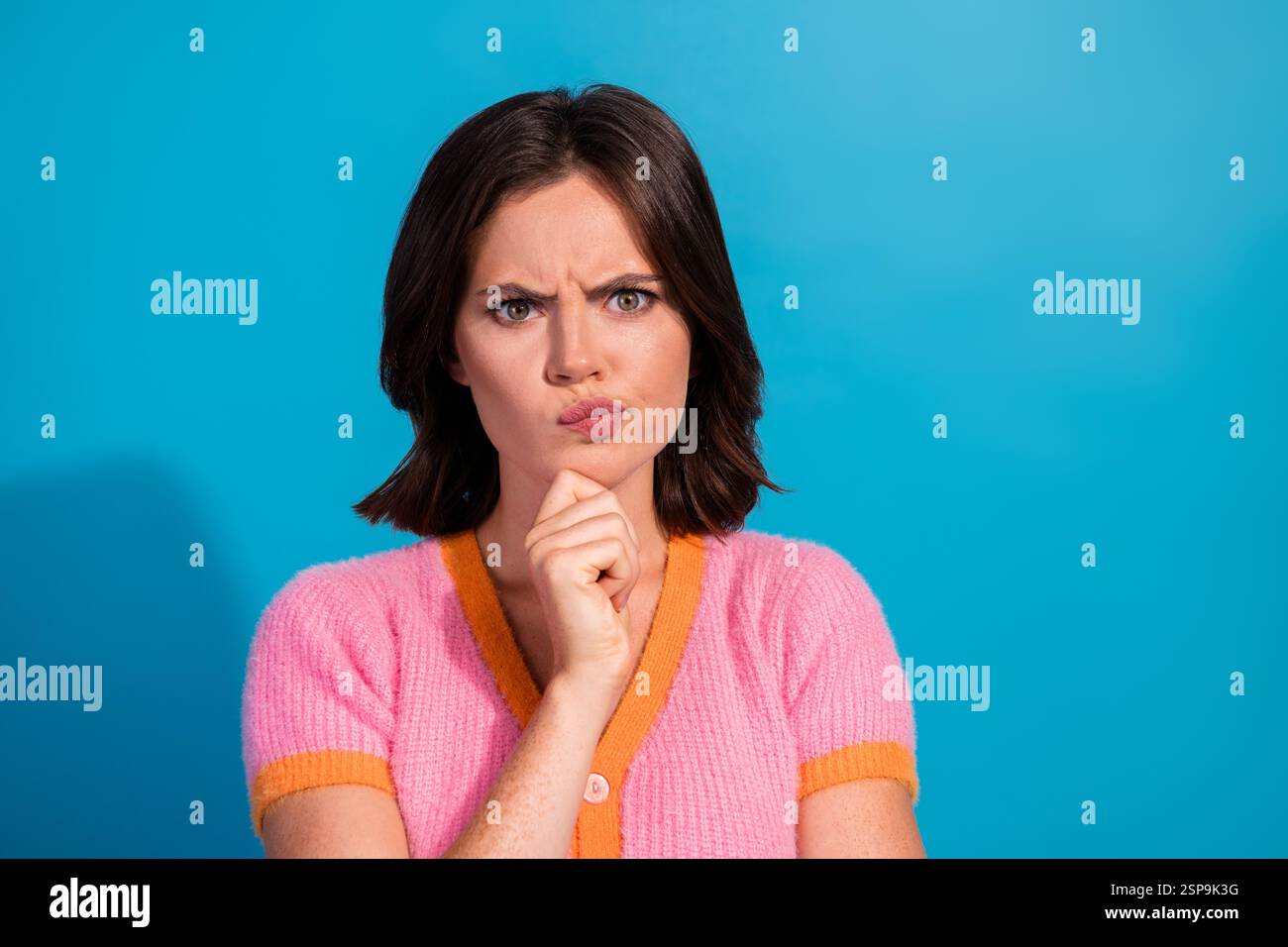 Thoughtful young woman with questioning expression against blue ...