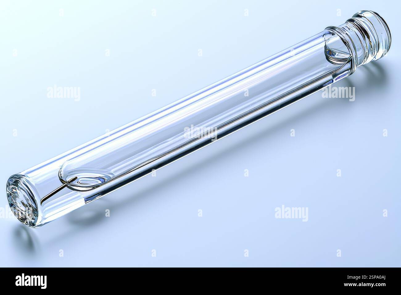 A clear glass tube lies on a reflective surface, highlighting its ...