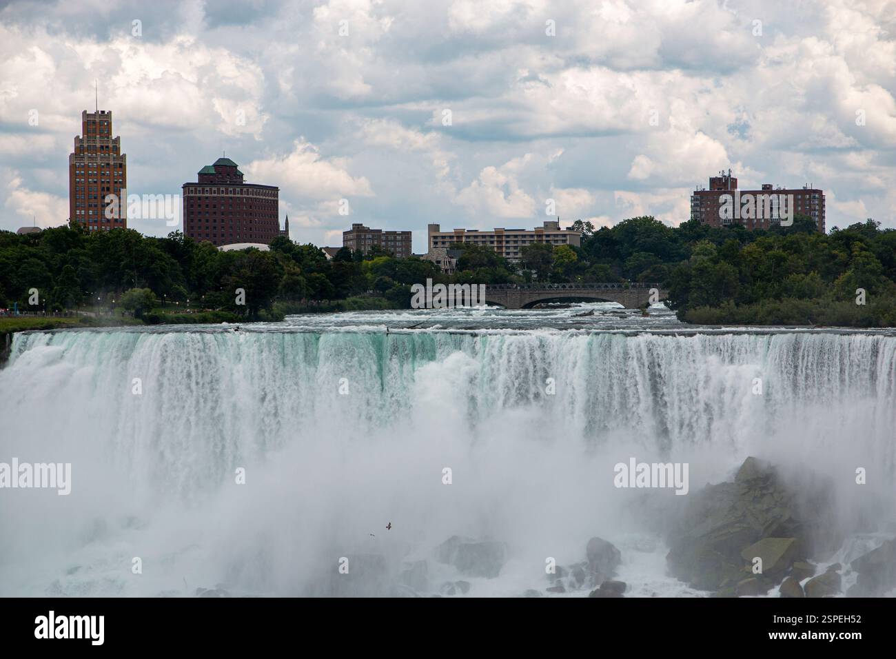 Powerful waterfalls rush down as buildings rise in the background under ...