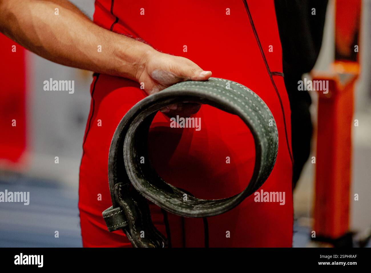 athlete powerlifter in a red singlet holds weightlifting belt behind ...