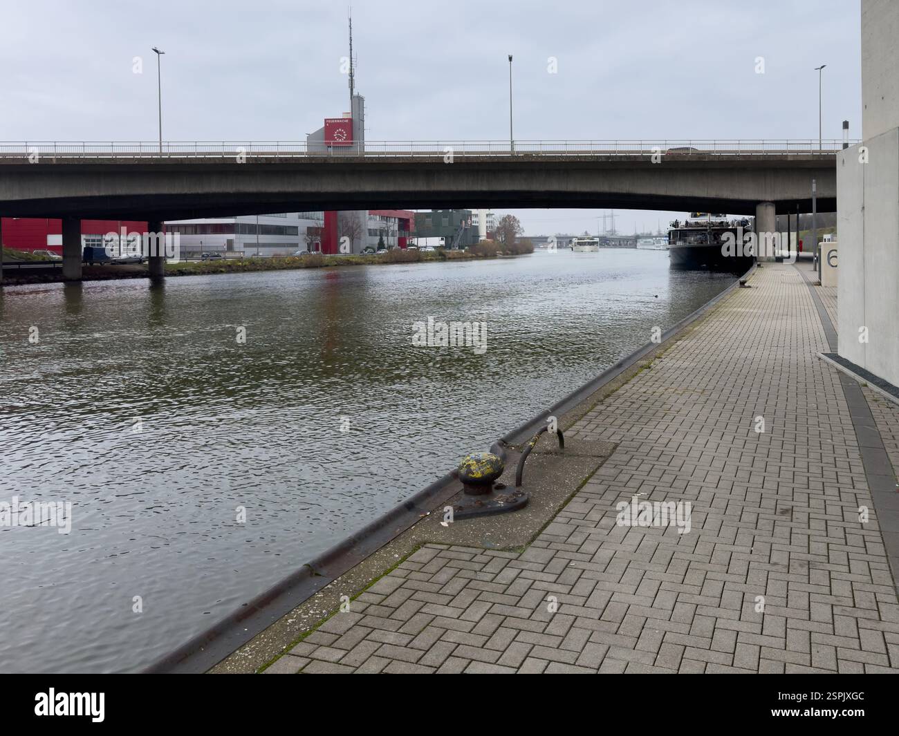 A gray concrete bridge spans a waterway with a docked barge visible. A ...