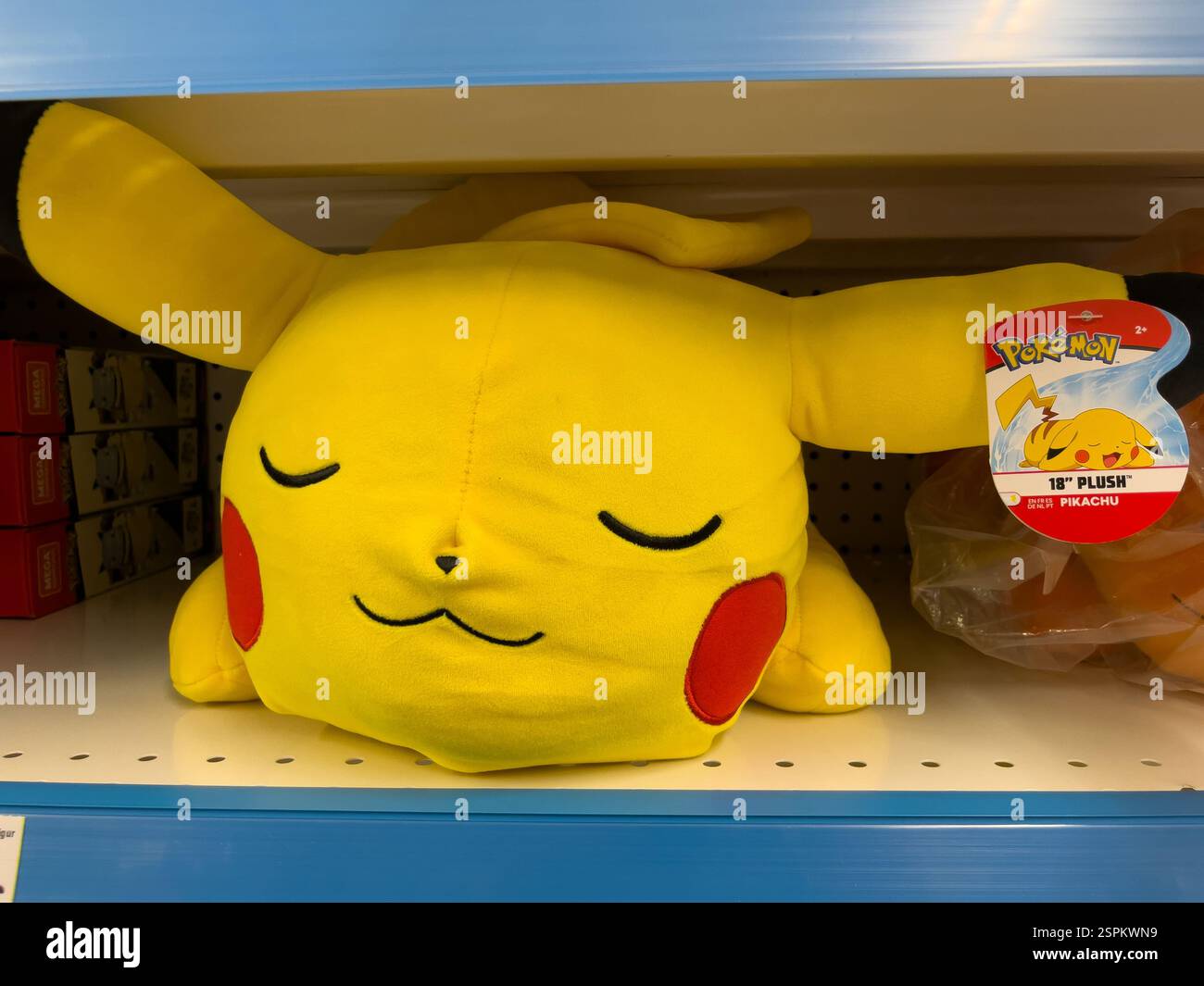 A large yellow Pikachu plush toy rests on a store shelf. The plush is ...