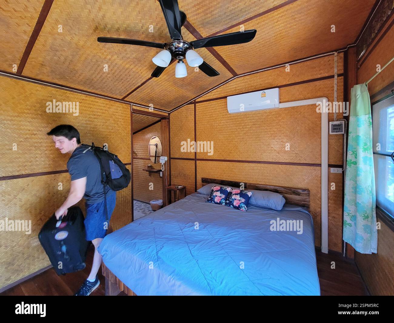 A man is carrying a suitcase while entering a bedroom with a fan Stock ...