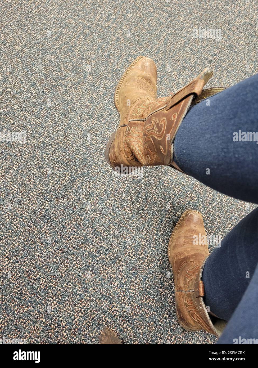 A person wearing stylish cowboy boots and blue jeans stands on a carpet ...
